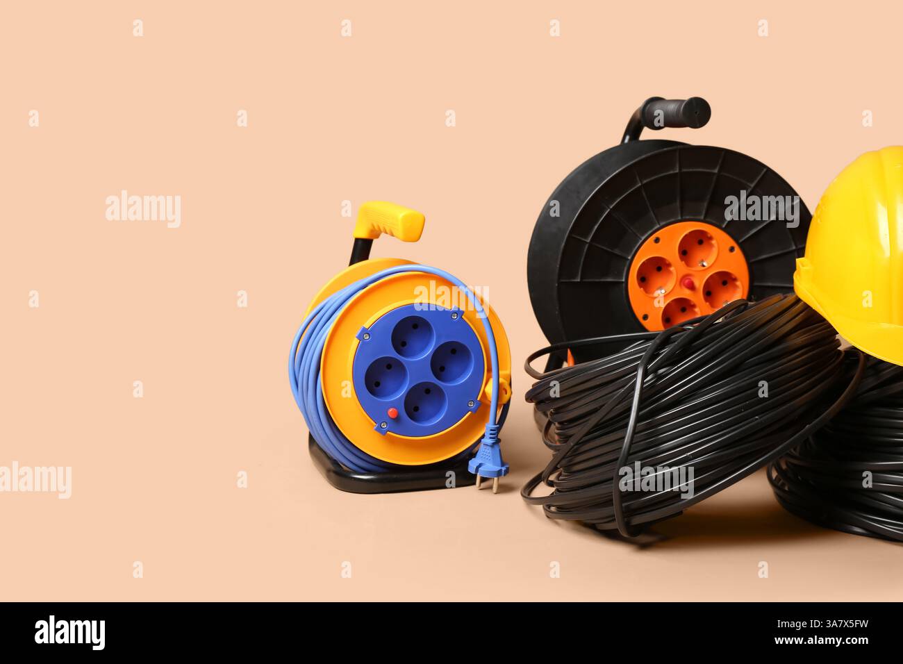 Rolled wires, hardhat and extension cable reels on beige background ...