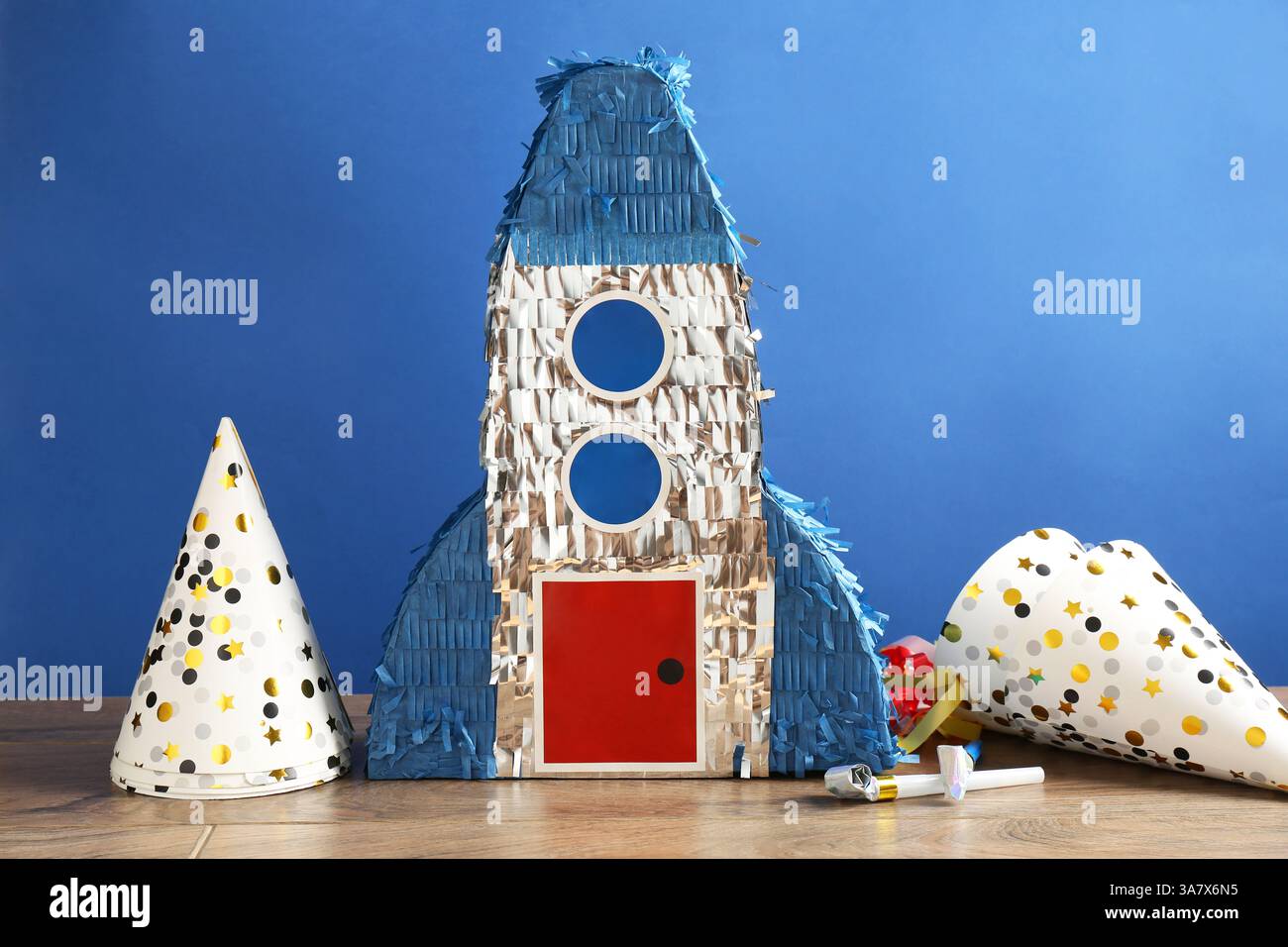 Beautiful pinata in shape of rocket, party cones and blowers on wooden ...