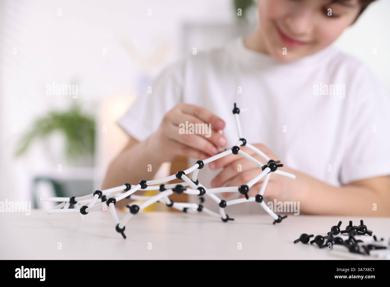 Boy making DNA structure model at desk indoors, closeup. Space for text ...