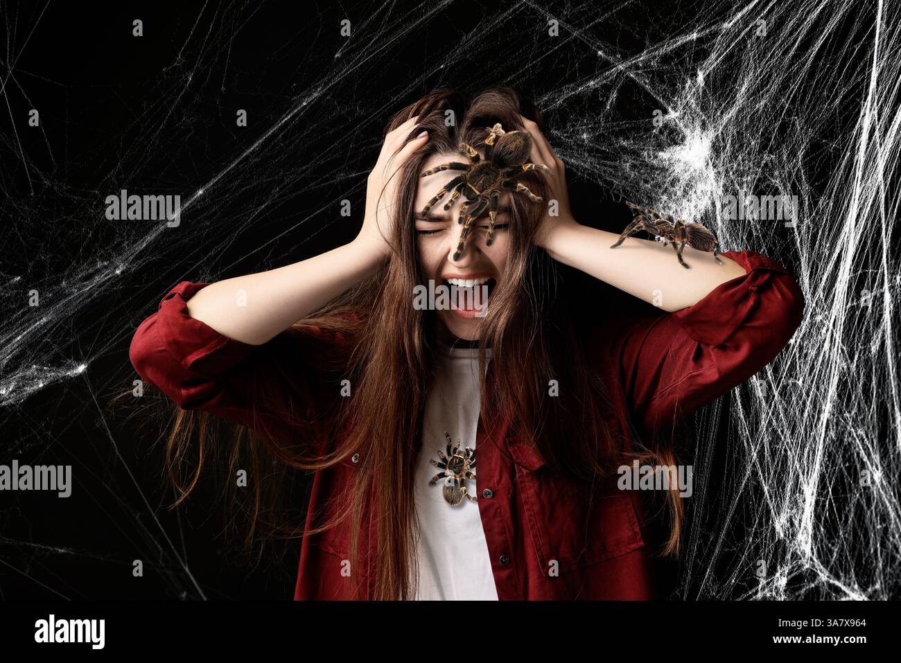 Scared woman with spiders and cobweb screaming against black background ...