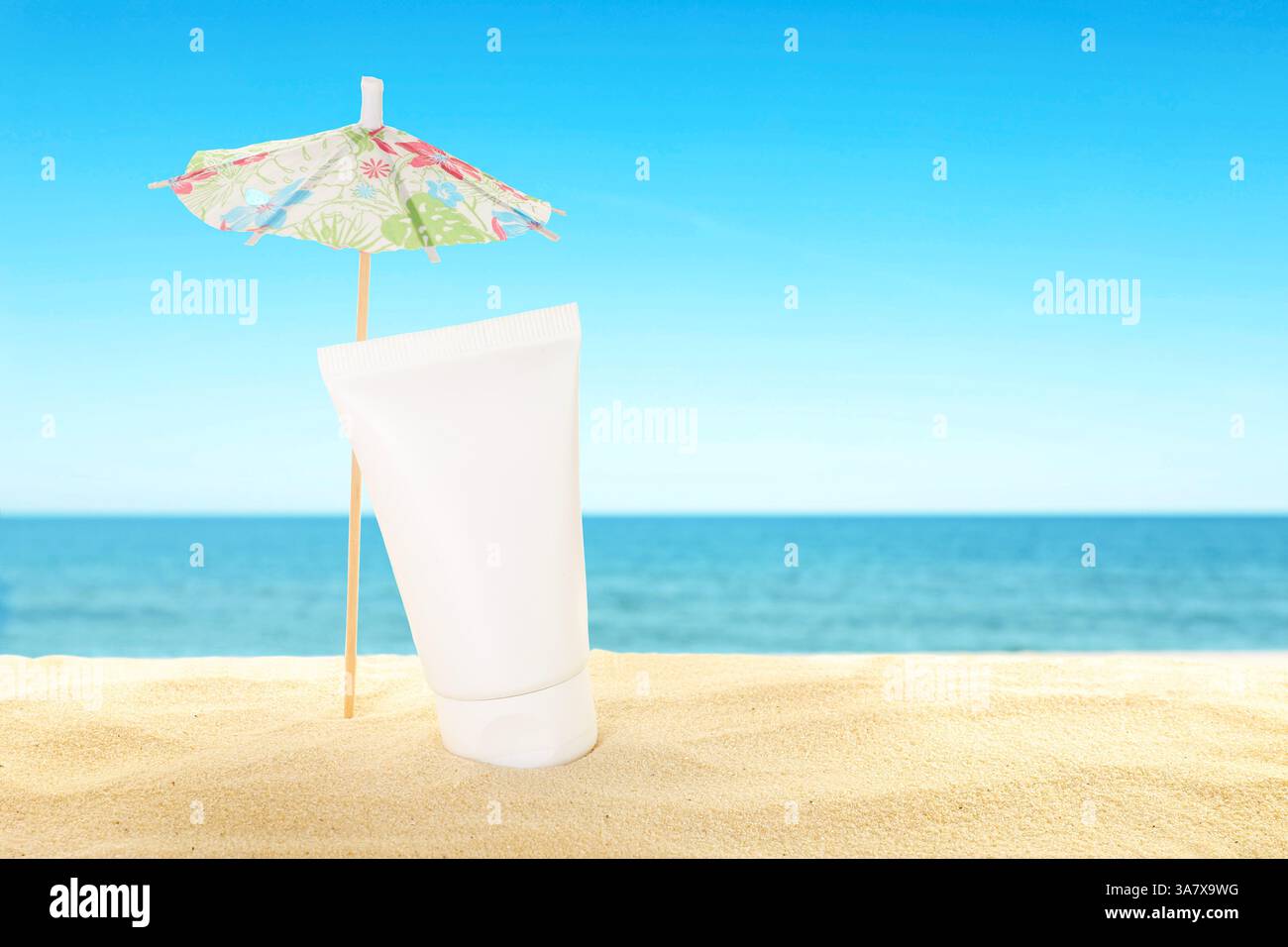 Tube of sunscreen product and cocktail umbrella on sandy beach near ...