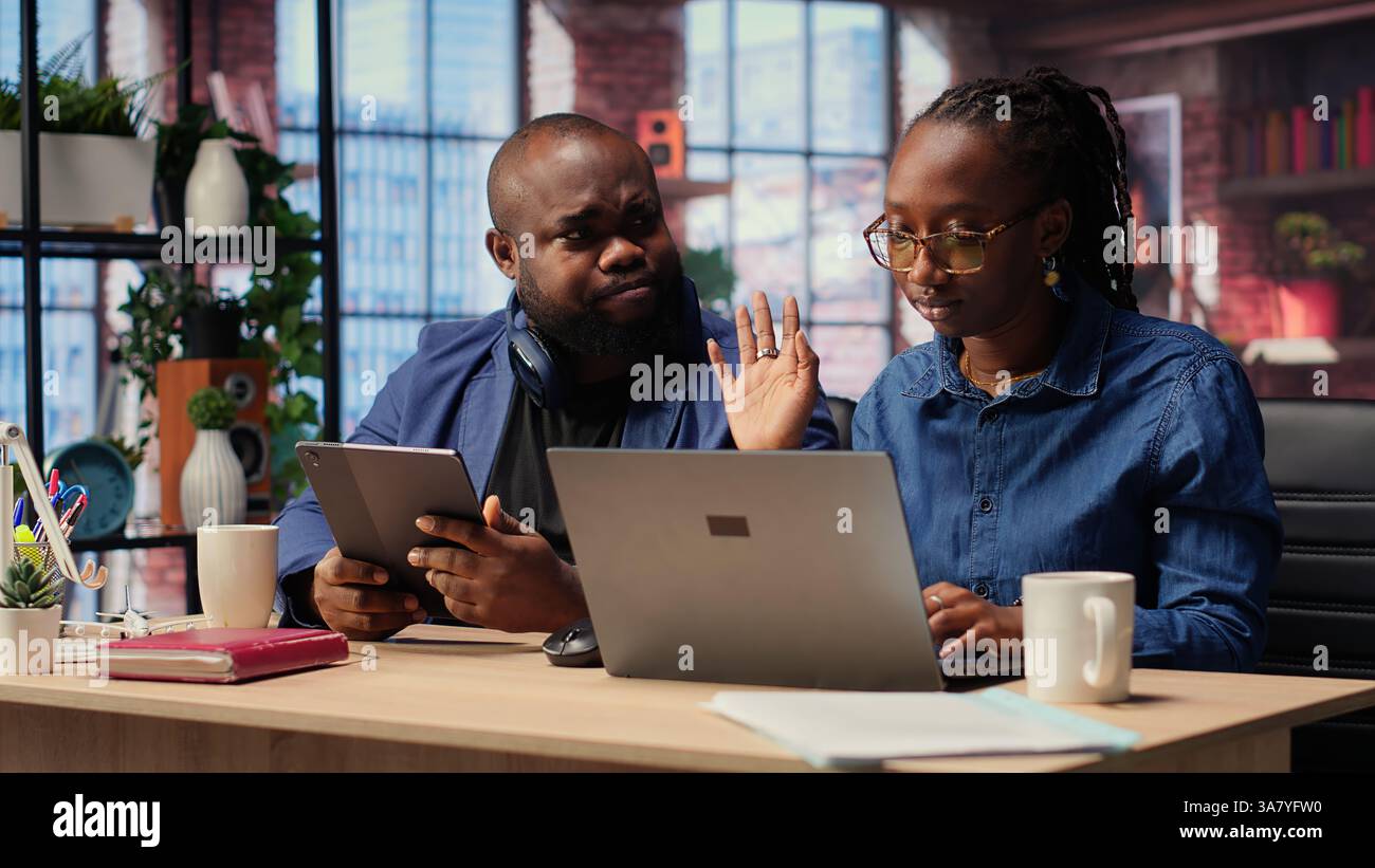 Black woman is working while her partner listens to music next to her, enjoying their time at ...