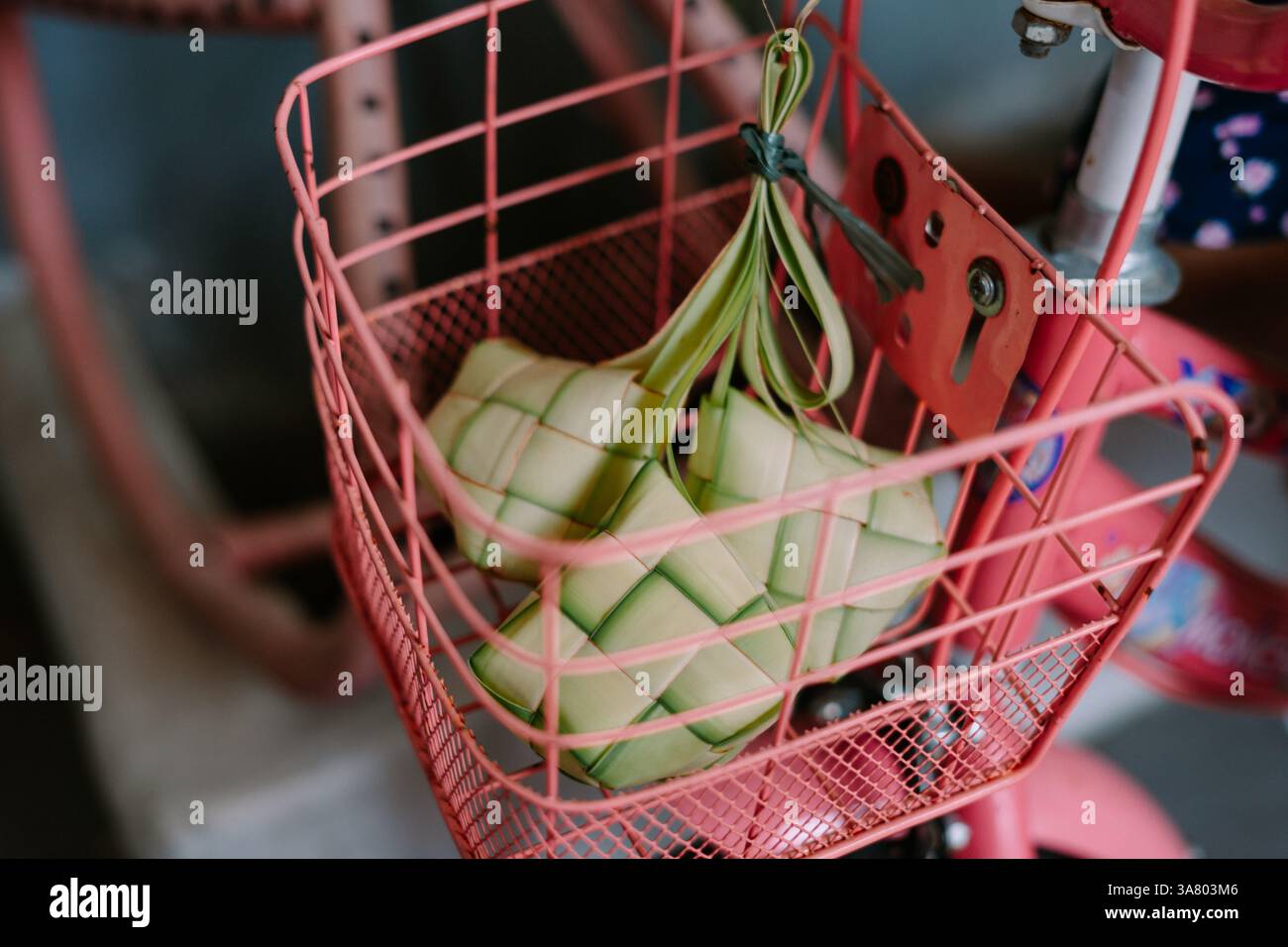 Ketupat, a traditional Malay rice dumpling, sits in a pink bicycle ...
