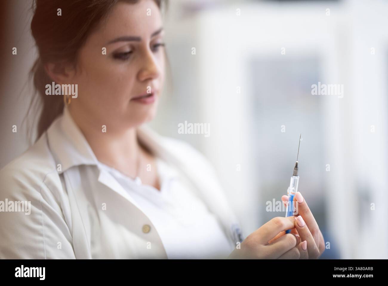 A focused nurse in a white lab coat carefully prepares a syringe for an ...