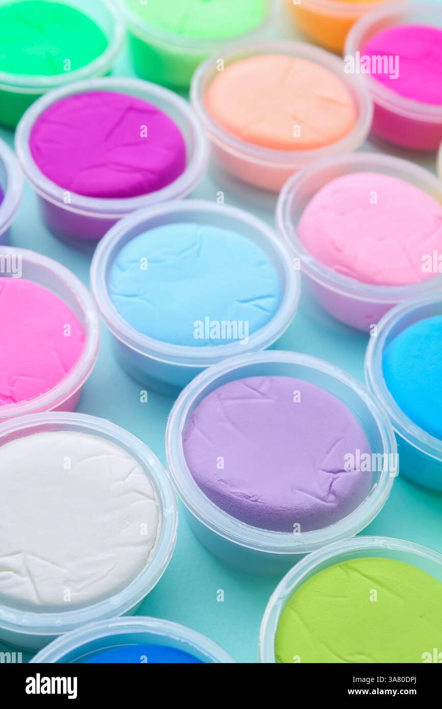 Different colorful modeling clay in plastic jars on light blue ...
