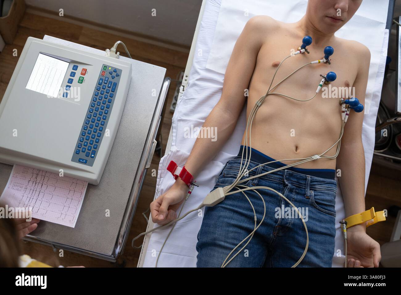 A female doctor performs an ECG on a young man in a hospital room ...