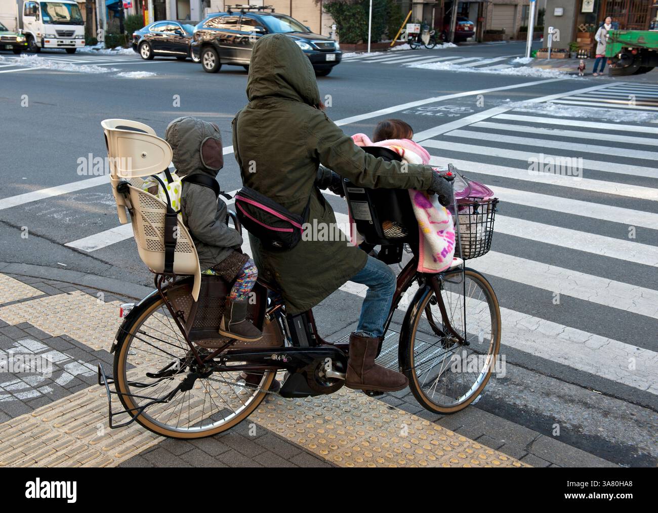 Mother rides through Tokyo streets on a bicycle with two children ...