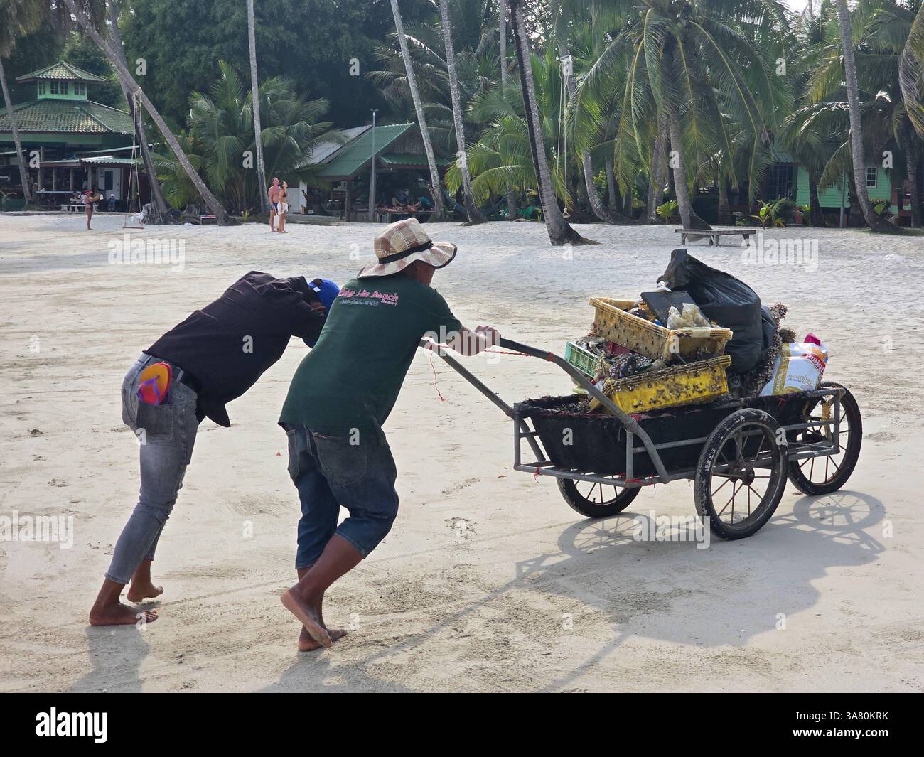 Koh Kood, Thailand, 13 March 2025, Two local men collaboratively push a cart loaded with rubbish ...