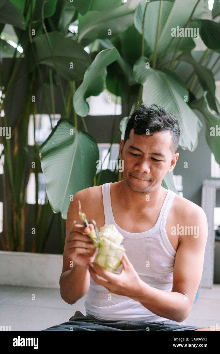 A man carefully trims a freshly cooked Ketupat. Ketupat is a rice ...