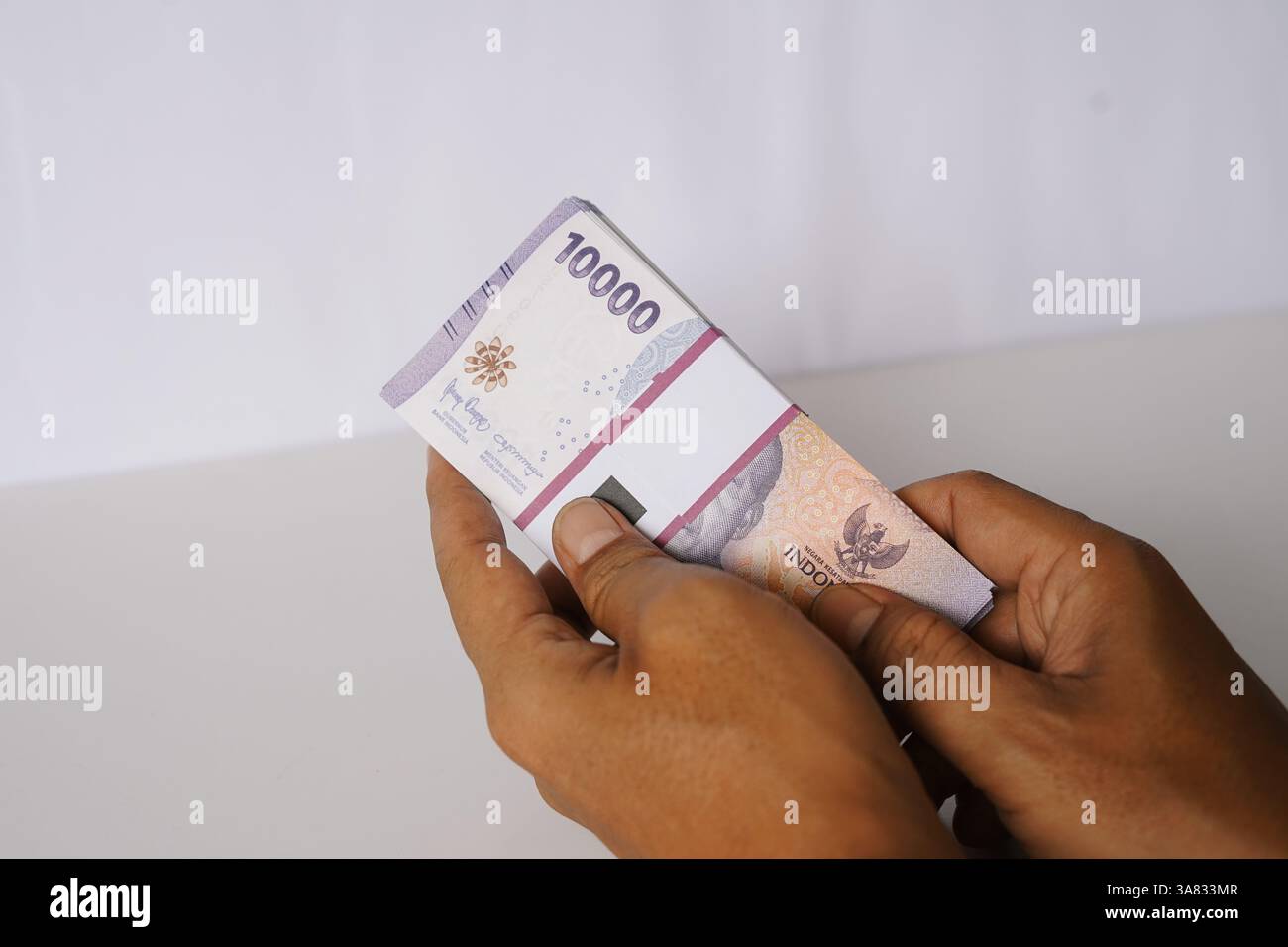 Close-up shot of a person's hands holding a stack of Indonesian Rupiah ...