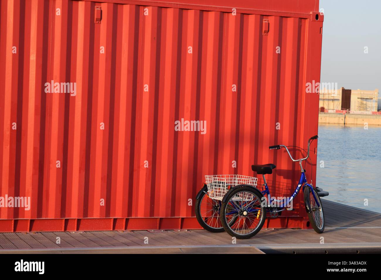 A vibrant tricycle rests by a bold red shipping container at the ...