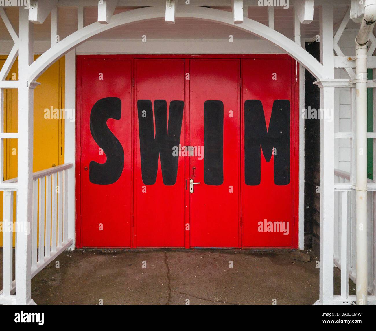 Beach chalet with red doors with the word ‘Swim’ painted in black ...