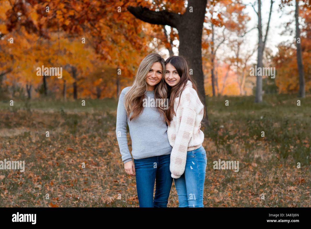 Mother and tween daughter stand together in pretty park on autumn day ...