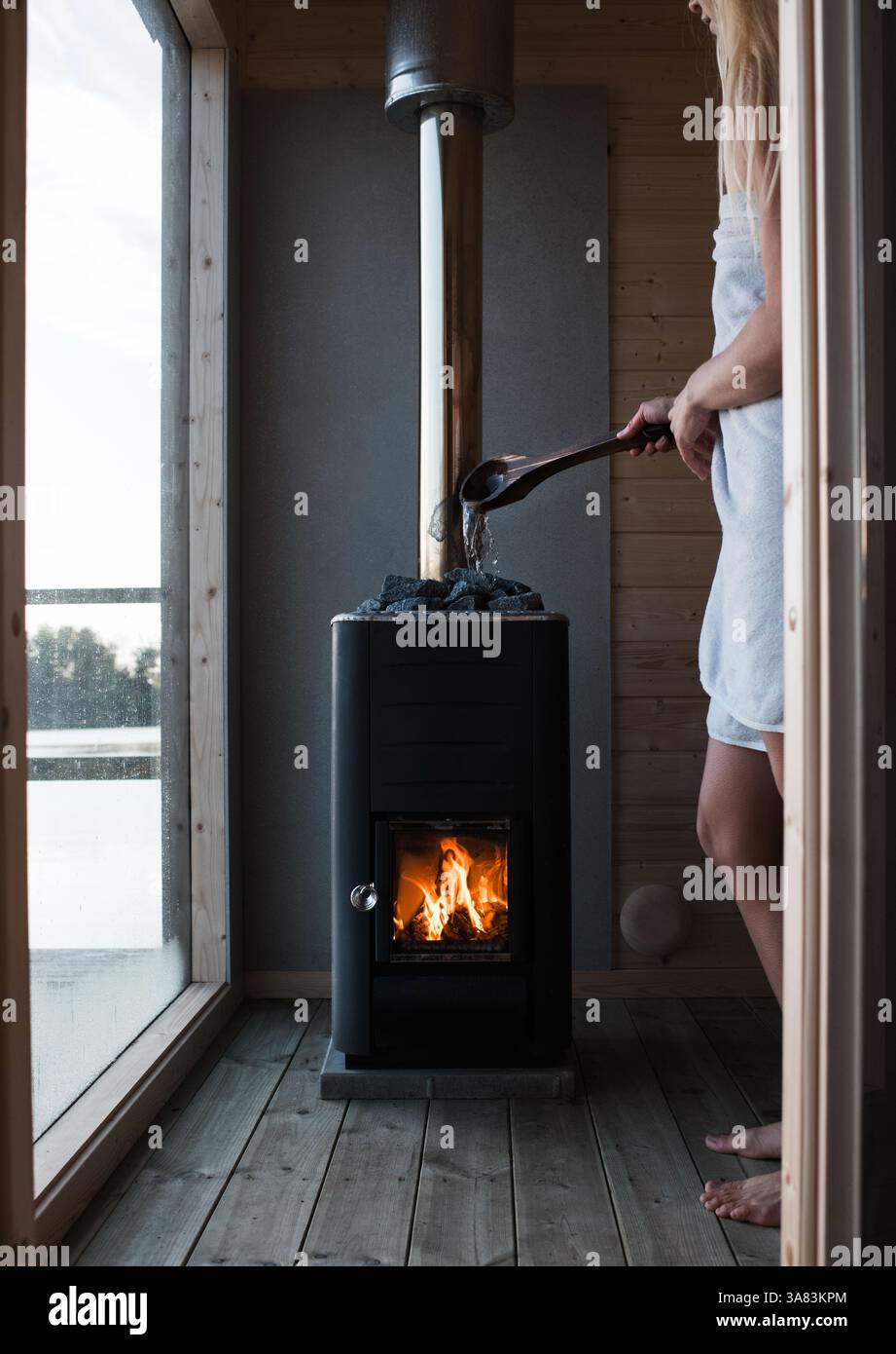woman pouring water onto hot coals on a fire wood burning sauna Stock ...