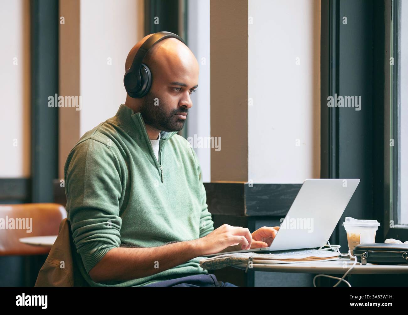 A man wearing headphones is working on his computer Stock Photo - Alamy