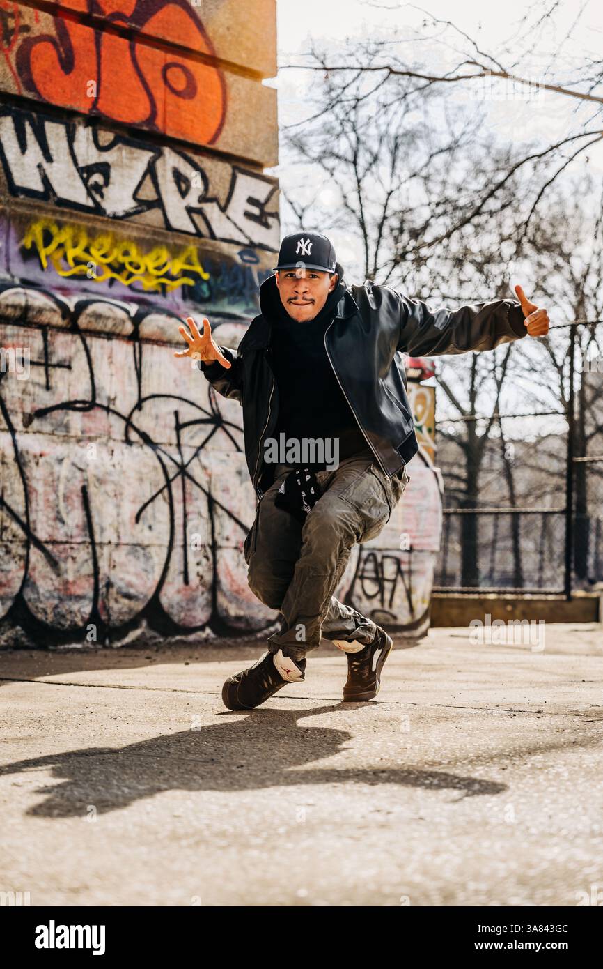 Street dancer strikes low dynamic pose near graffiti-covered wall Stock ...