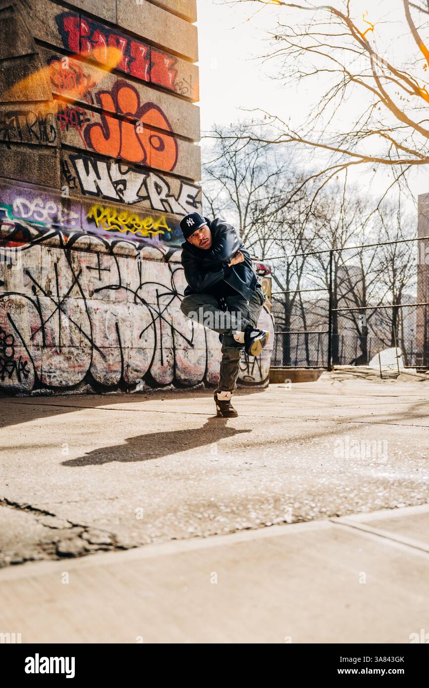 Street dancer balances in pose by graffiti wall in bright sunlight ...