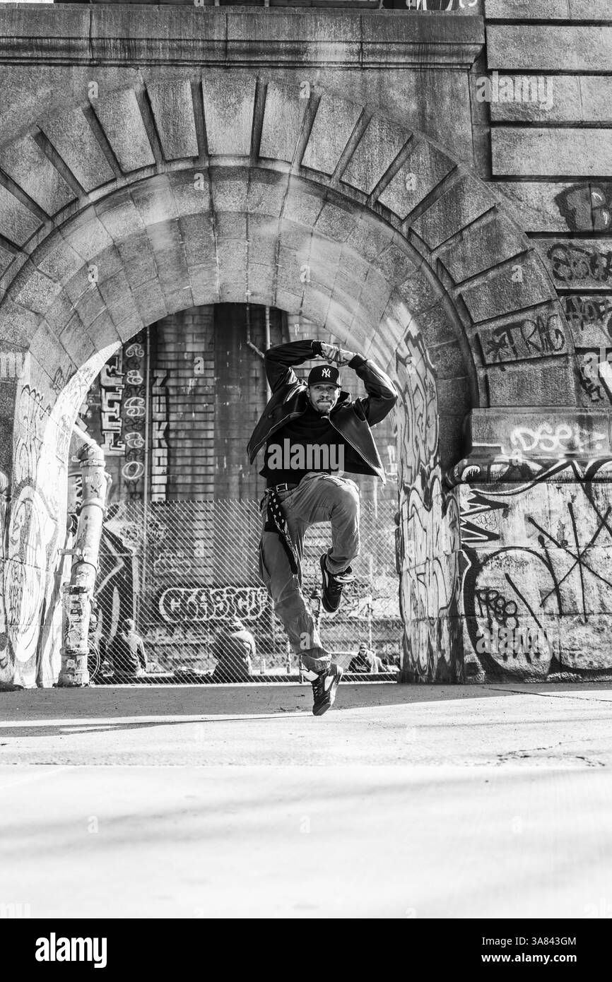 B-boy mid-jump under arched bridge in gritty black-and-white scene ...