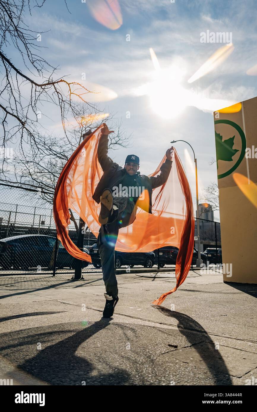 Dancer kicks high with orange fabric flaring under bright sunlight ...
