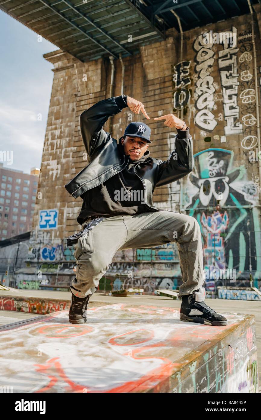 Street dancer strikes pose on graffiti-covered ledge under bridge Stock ...