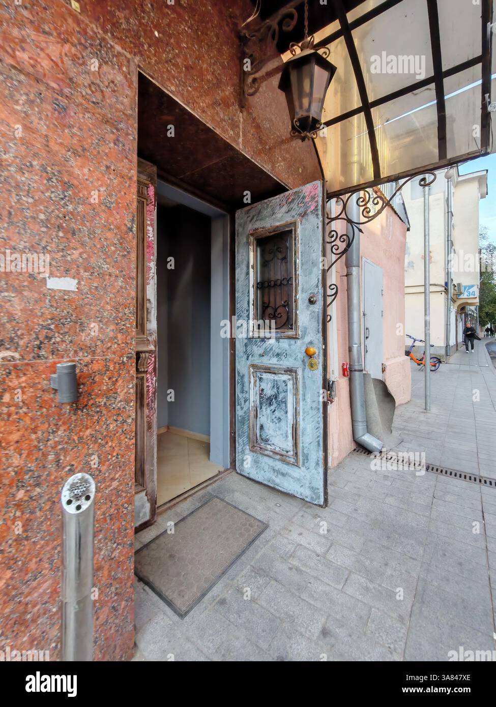 An aged, weathered wooden door with peeling paint set in a red marble facade, under a decorative ...