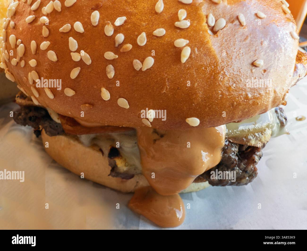 Close-up of a juicy hamburger dripping with sauce, featuring a sesame ...