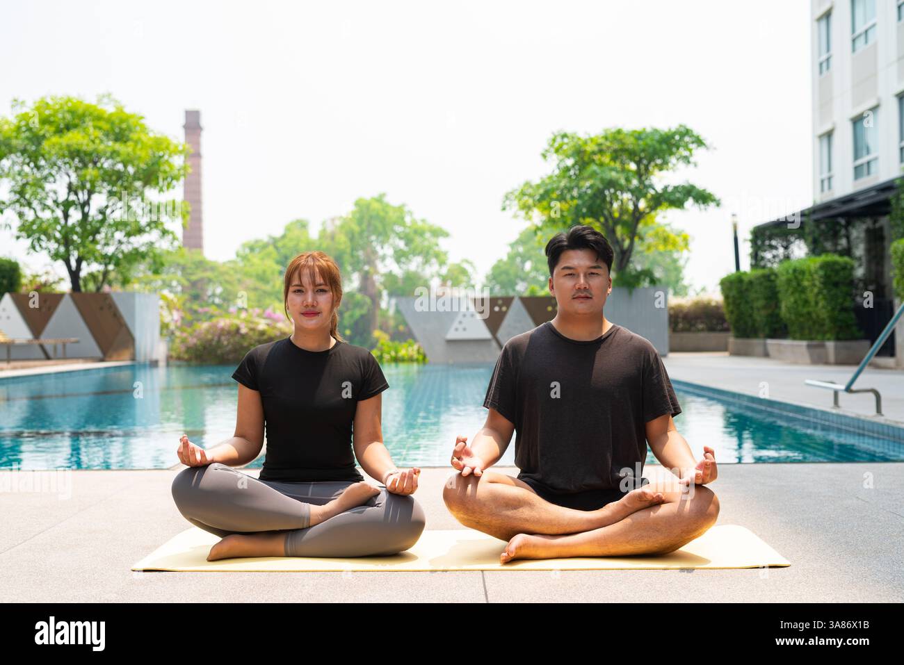 Young Asian couple doing yoga exercise next to swimming pool during ...