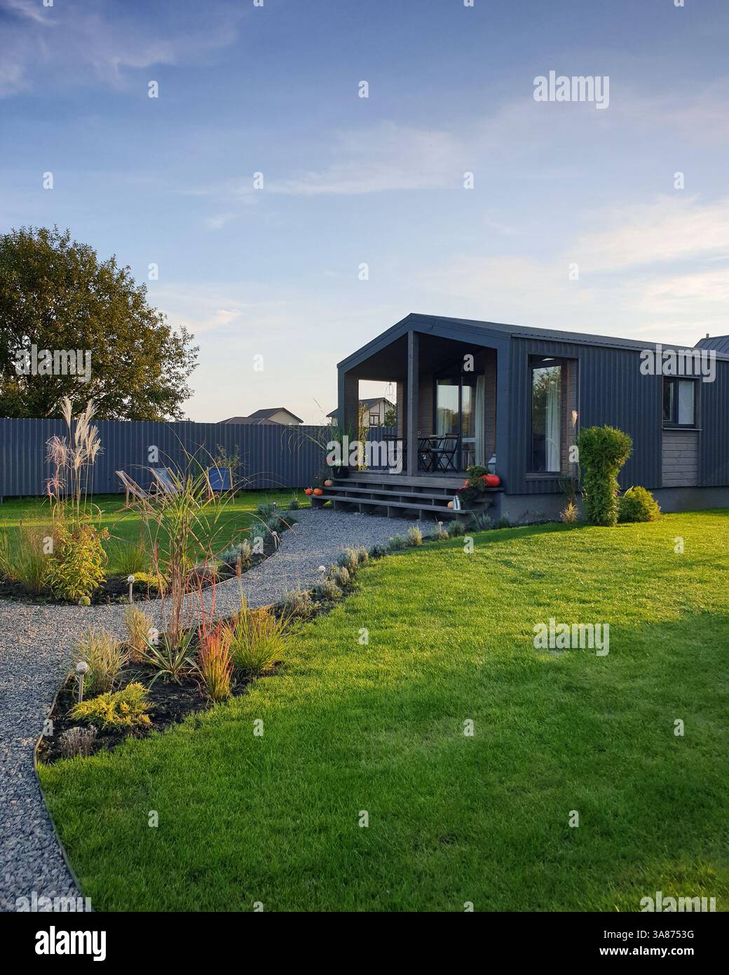 Modern summer house in rays of morning sun, lawn and fenced yard around ...