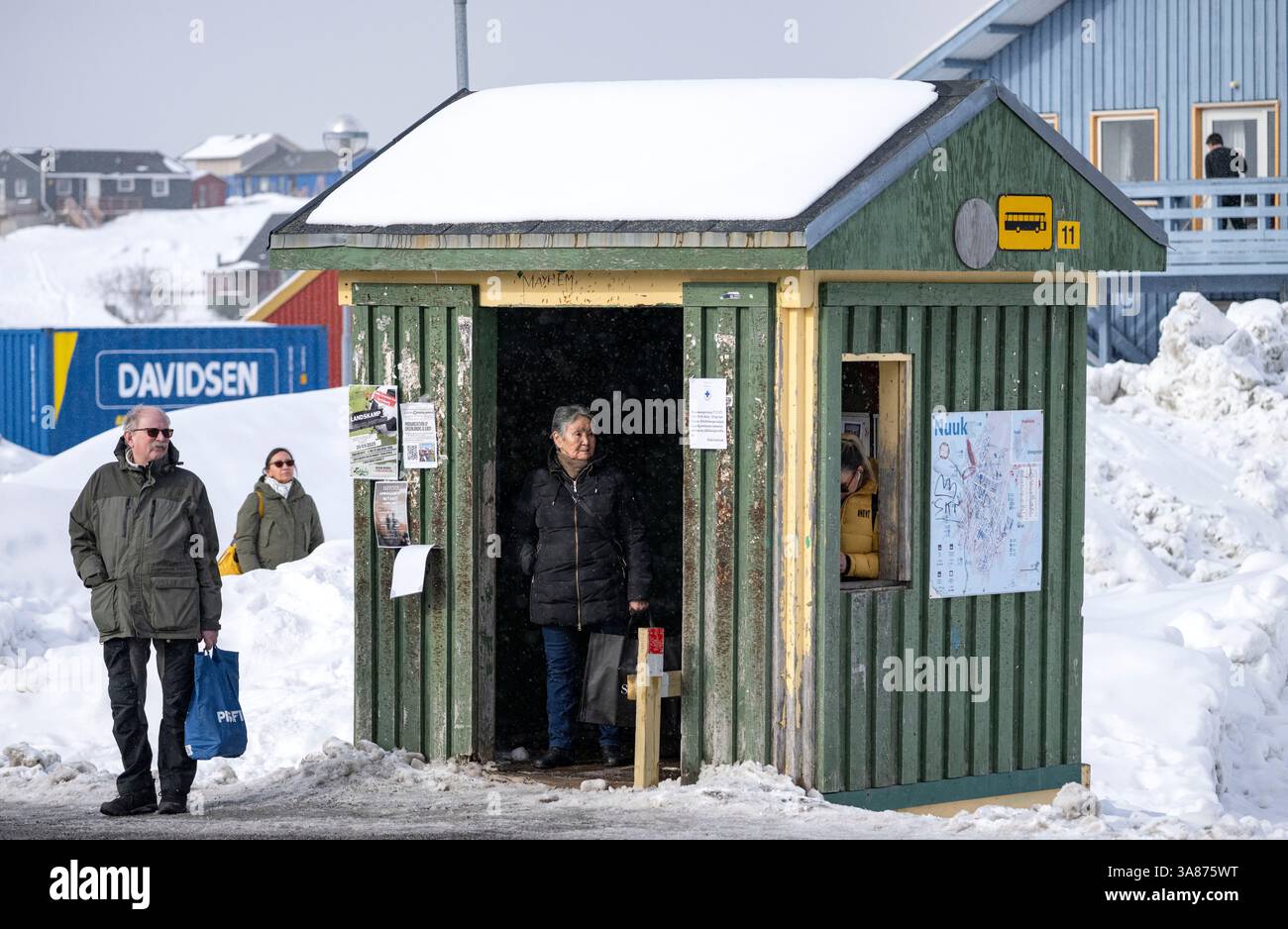 Passengers wait for one of the yellow city buses at a bus shelter in ...