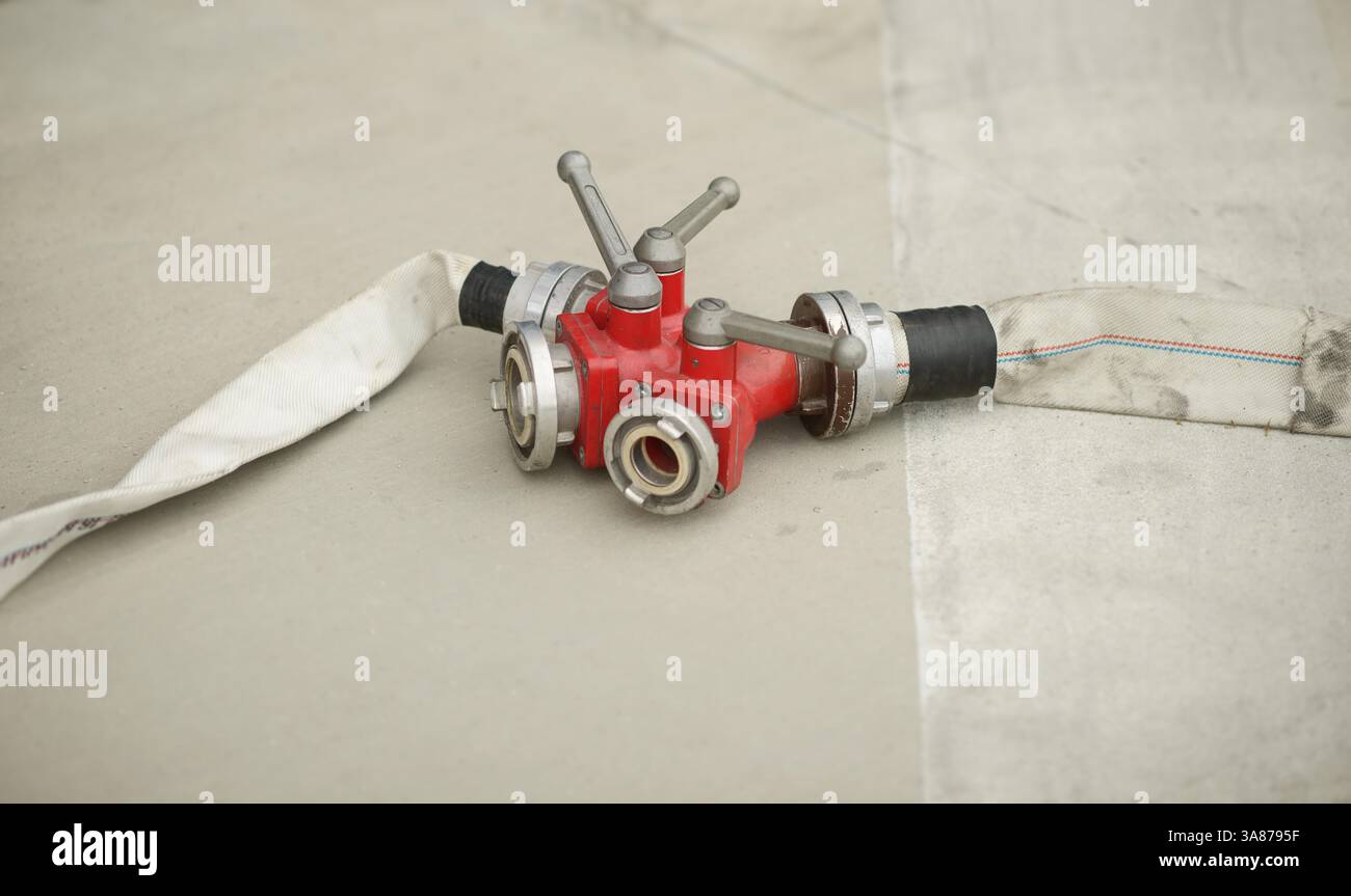 A red fire hose splitter with three metal valves lies on a concrete ...