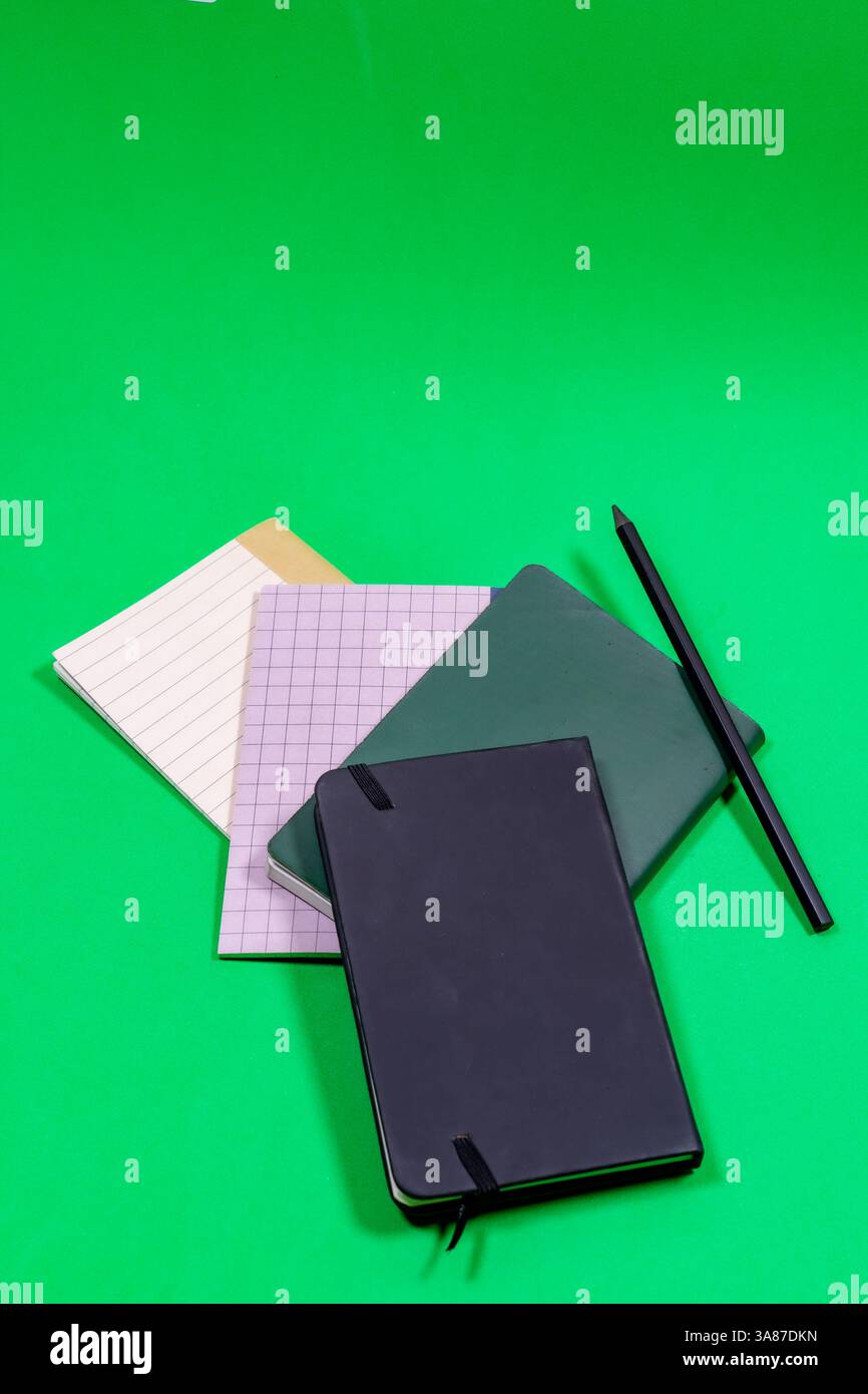 Different types of colored notebooks with a black pen on a green ...