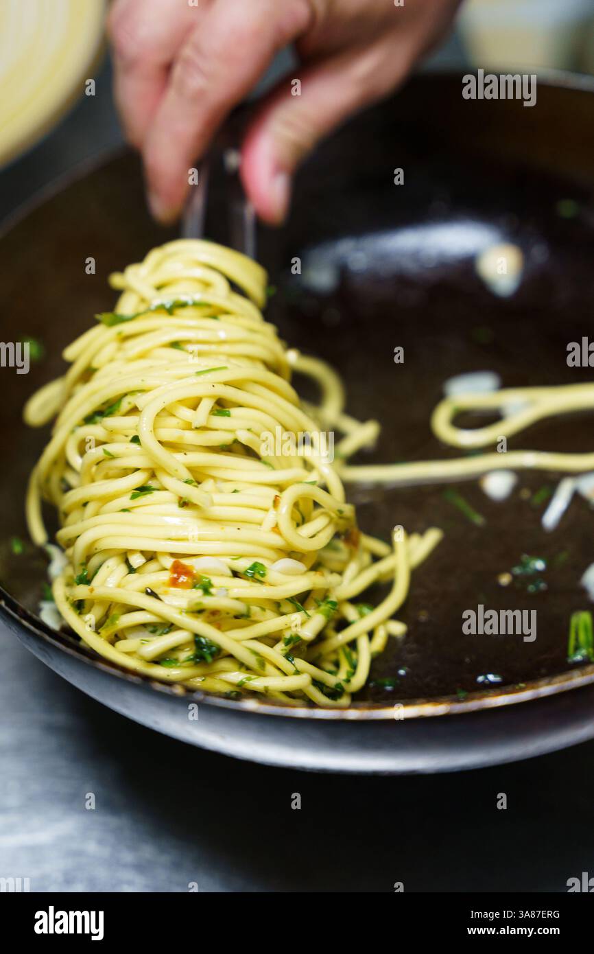 A close-up shot of freshly cooked spaghetti aglio e olio being lifted ...