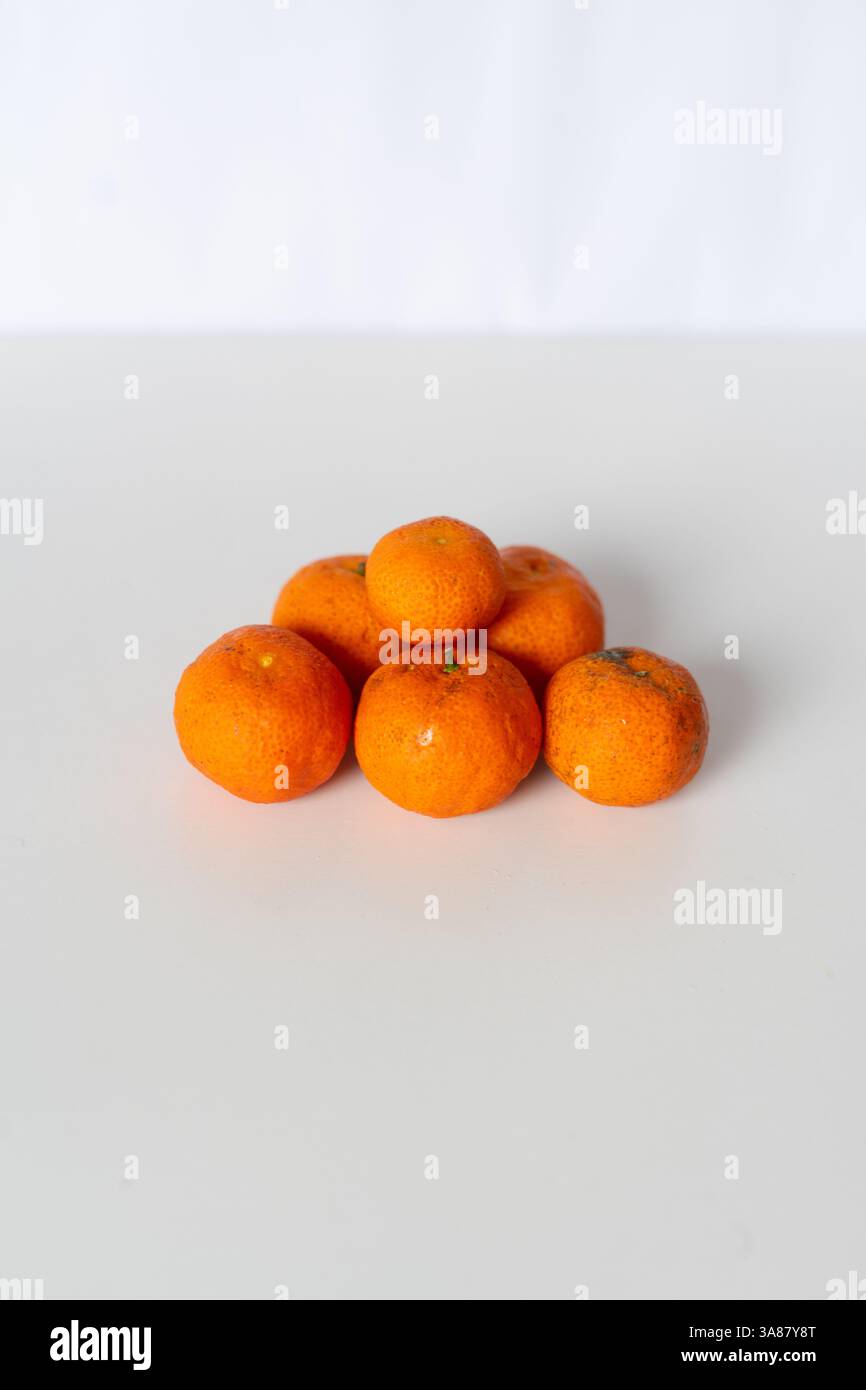 A group of mandarin oranges piled together on a white surface. The ...