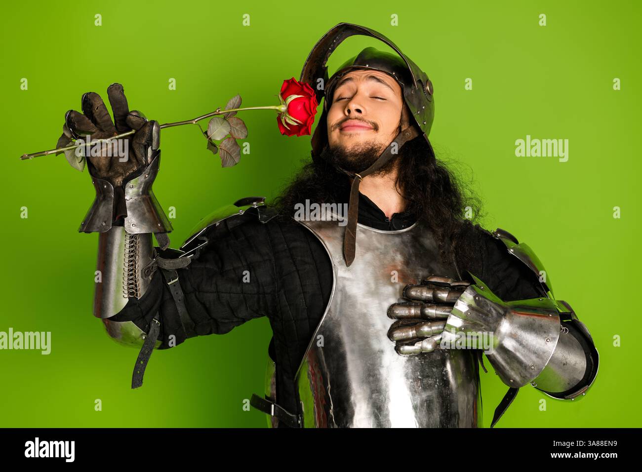 Medieval knight wearing armor holding a red rose against a bright green ...
