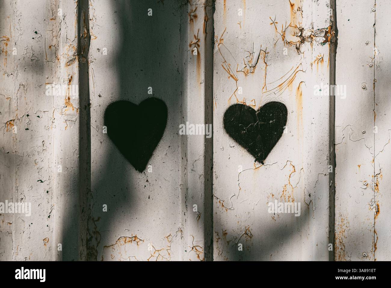 Two black heart shapes spray painted on cracked white wall with peeling ...