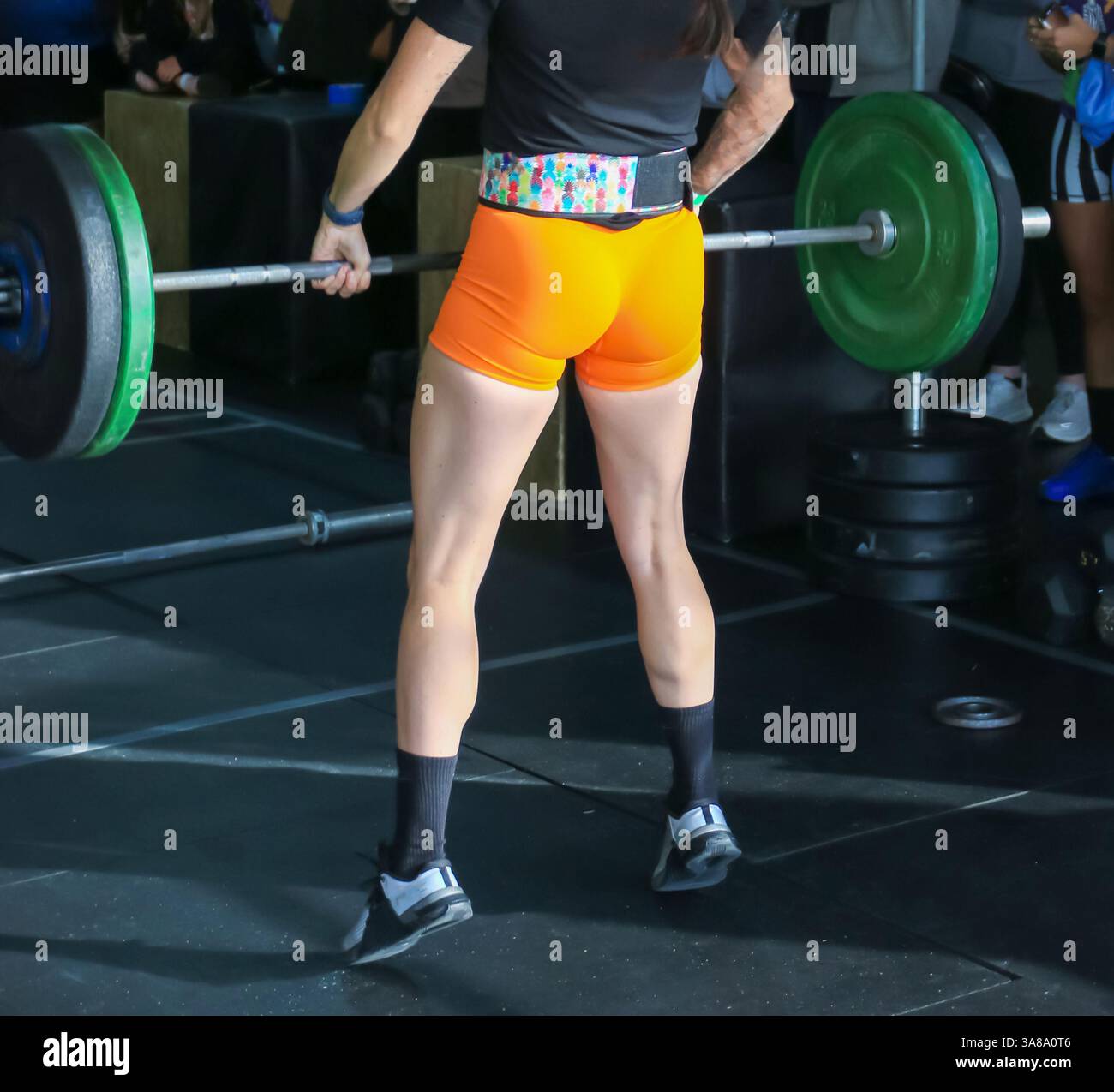 A female athlete focuses on lifting a heavy barbell in a gym during ...