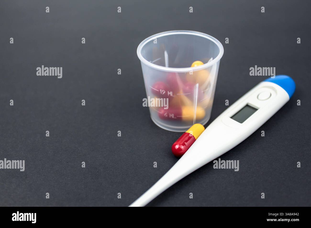 Medical capsules, tablets and clinical thermometer inside measuring cup ...