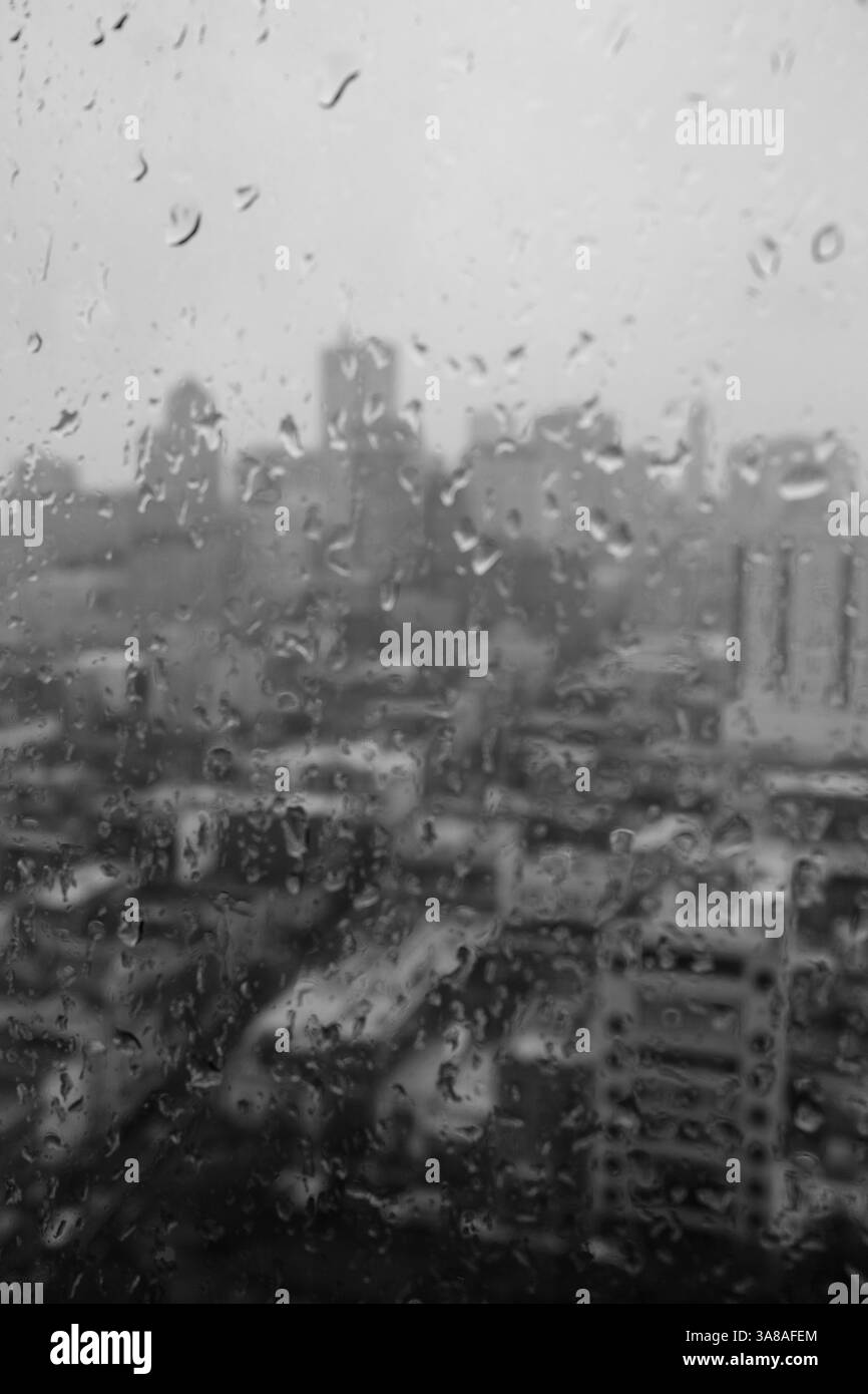 Raindrops on a window obscure the view of the city skyline on a gloomy ...