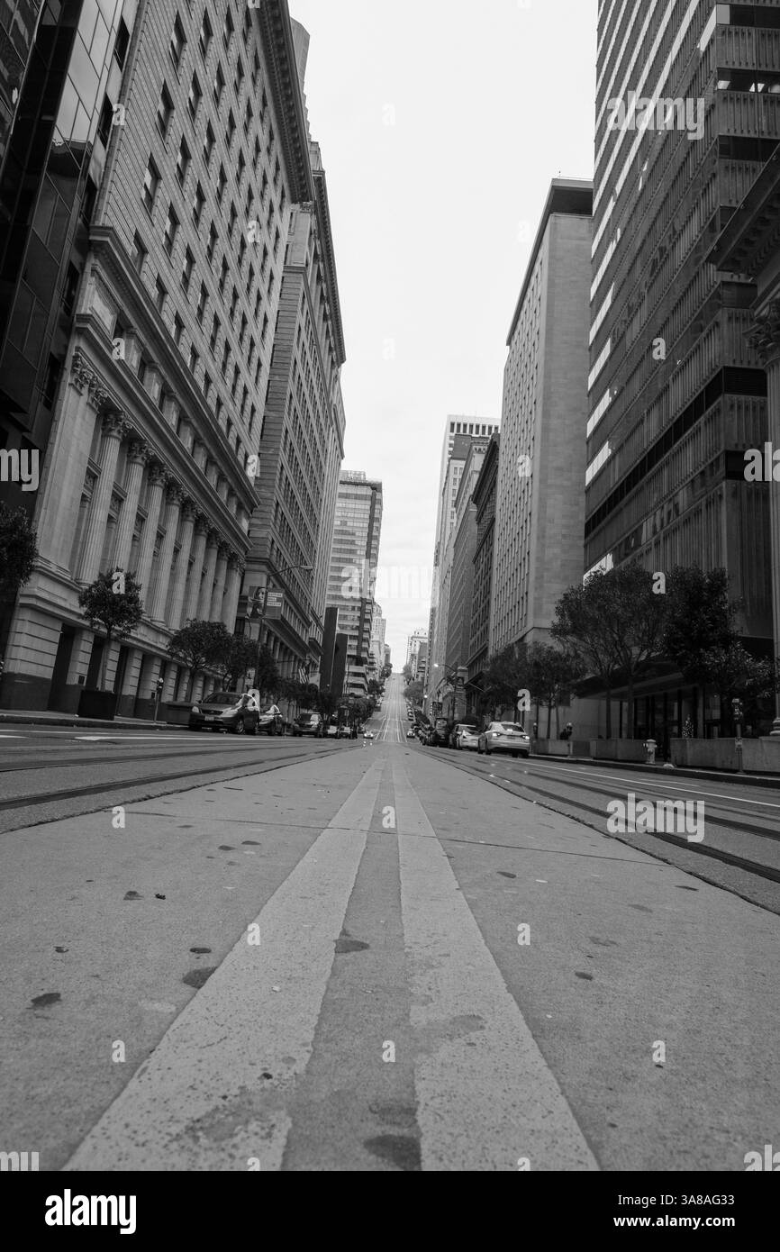 A low-angle, black and white view looks up a steep city street lined ...