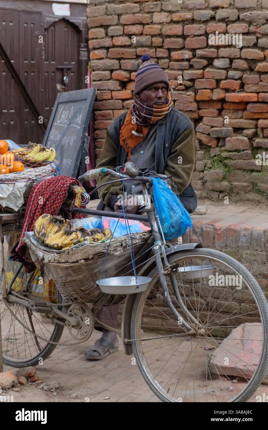 A fruit vendor sits beside his bicycle stall, equipped with scales and ...