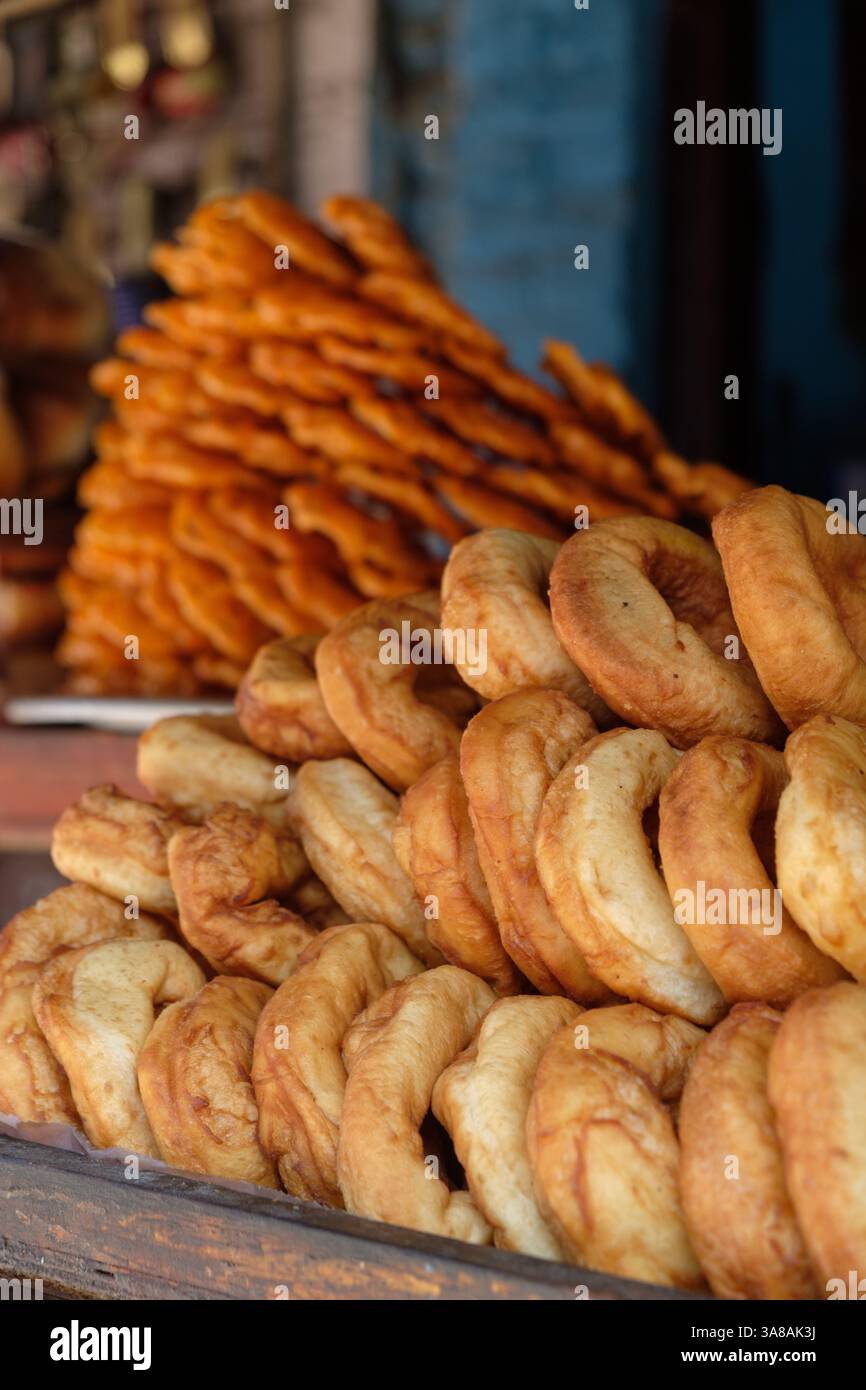 Stacks of fried ring-shaped and twisted pastries are displayed for sale ...
