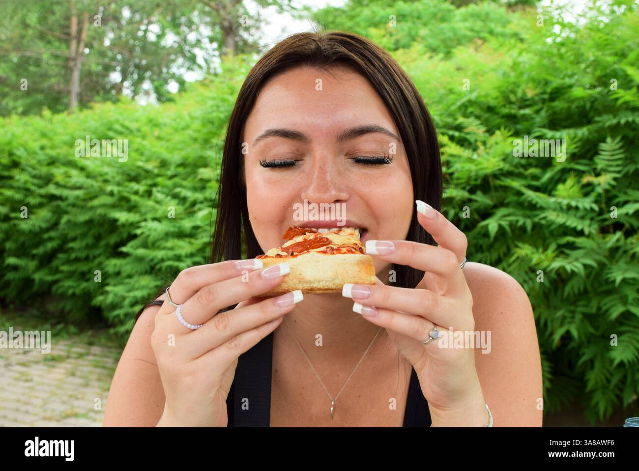 Closeup young woman biting pepperoni pizza slice outdoors Stock Photo ...