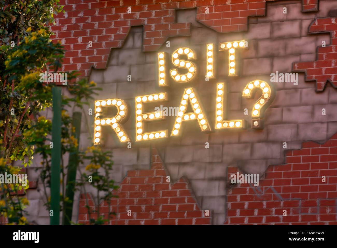 A weathered brick wall with a lit-up sign reading "IS IT REAL?" against ...