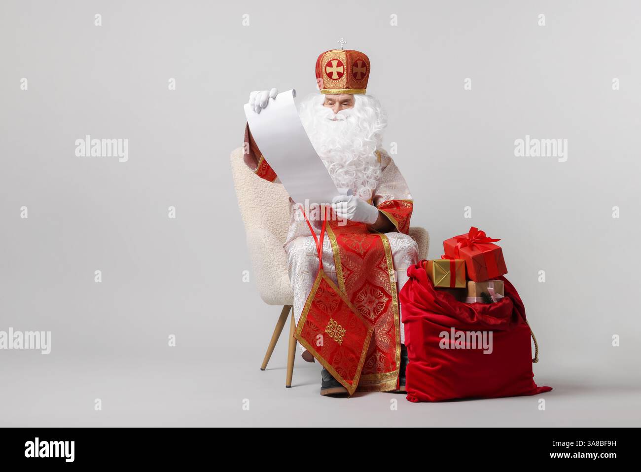 Saint Nicholas with wish list and sack full of gifts on light grey ...