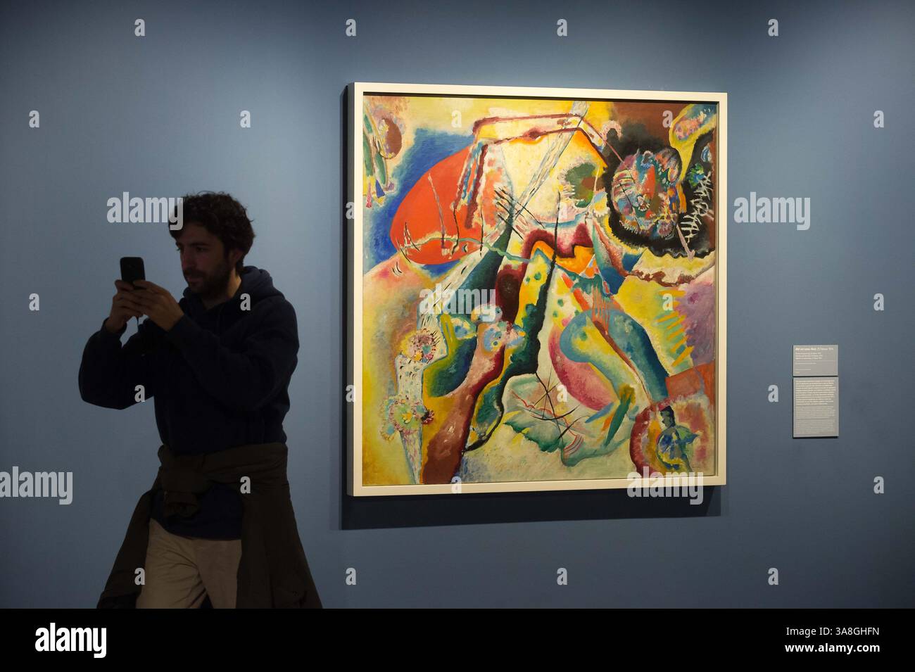 A man takes a photo next to a painting title: "Vassily Kandinsky ...