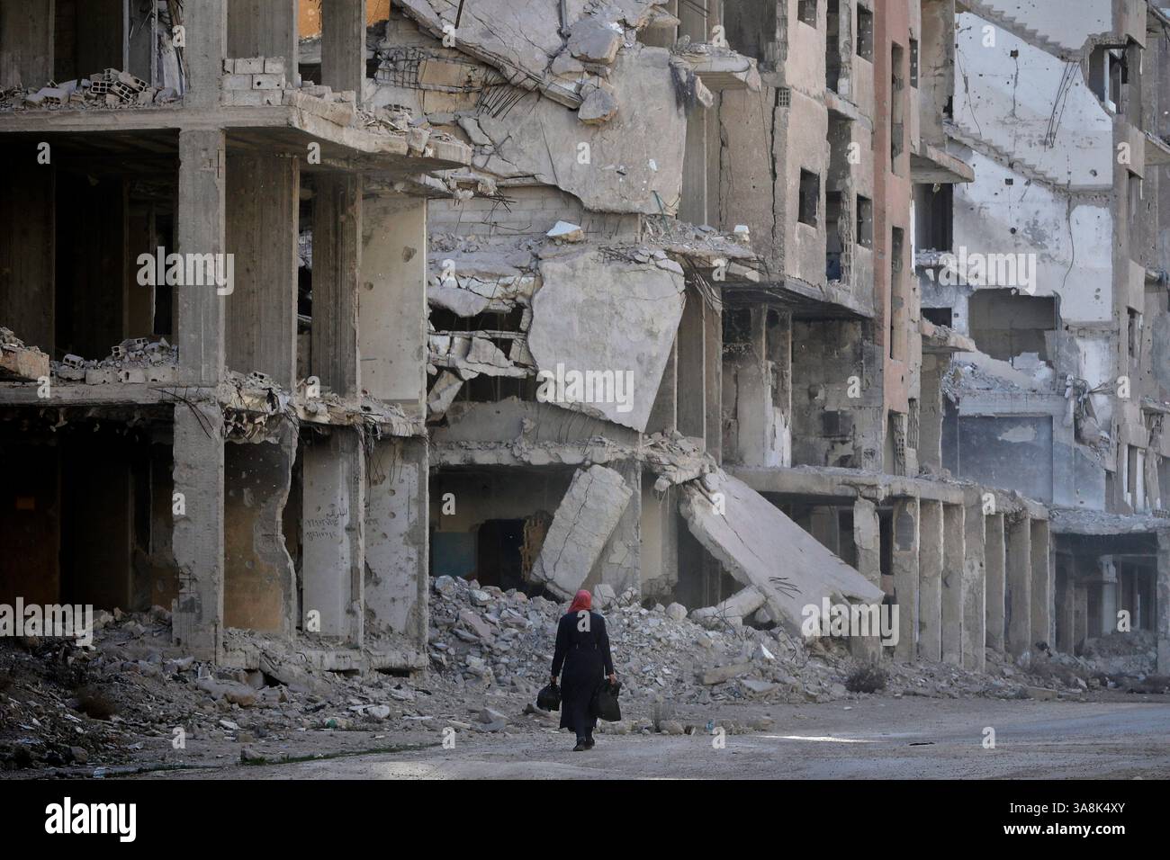 A woman walks past damaged apartment buildings in Daraya, Syria ...