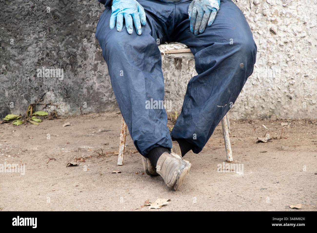 Dirty male painter in working uniform in paints sits on a chair on the ...