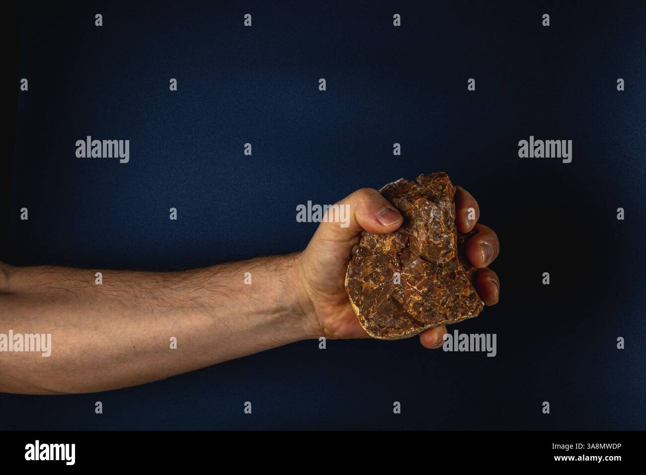 A person's hand grips a rugged rock tightly, highlighting the texture ...
