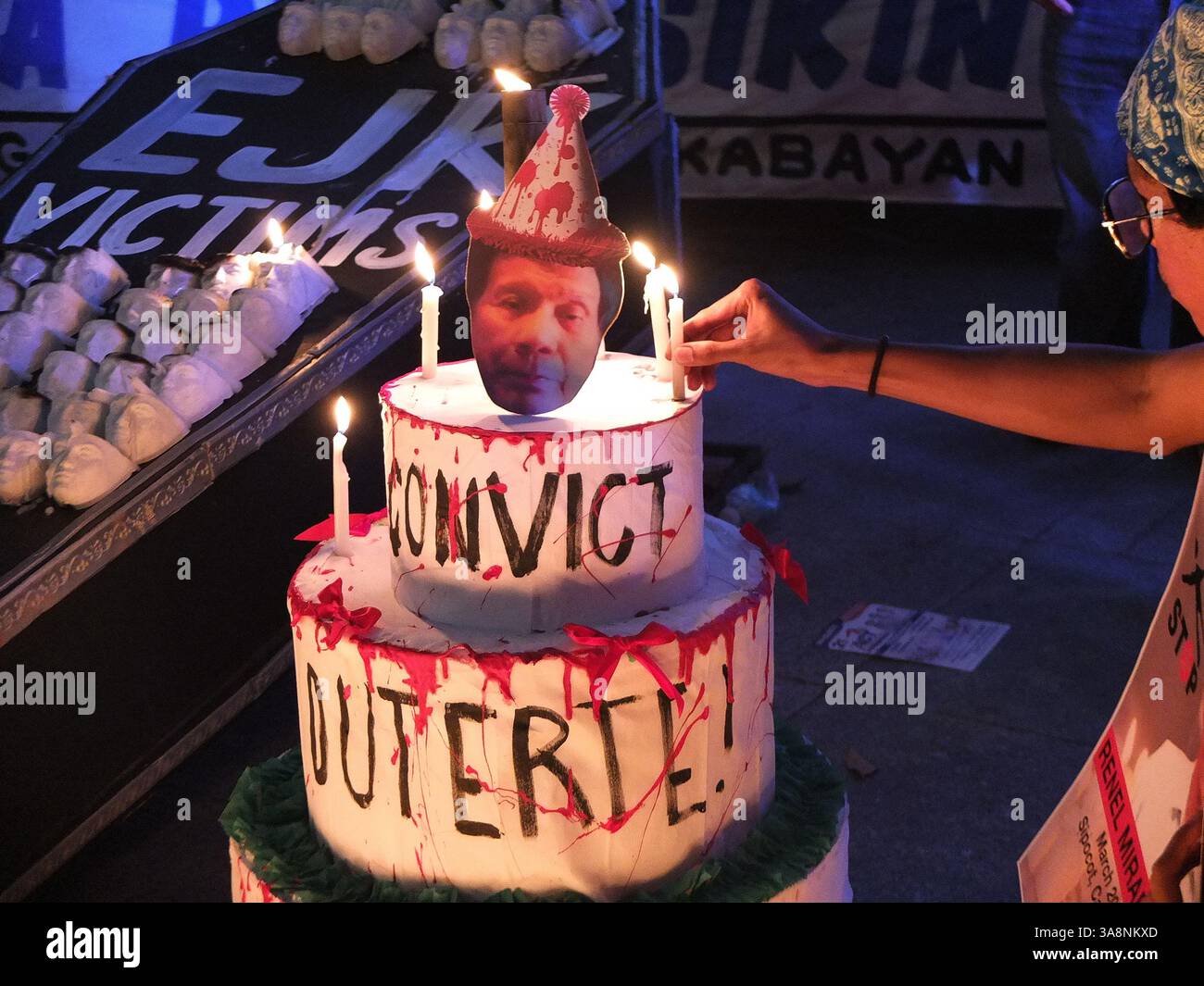 A protester lights a candle ontop of a paper cake with a picture of ...