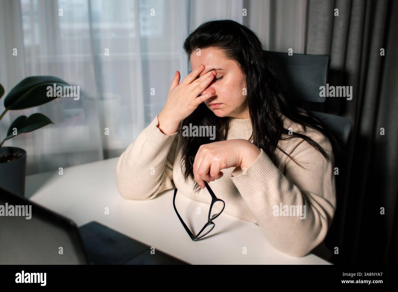 Tired woman working at home with laptop holding eyeglasses rubbing eyes ...